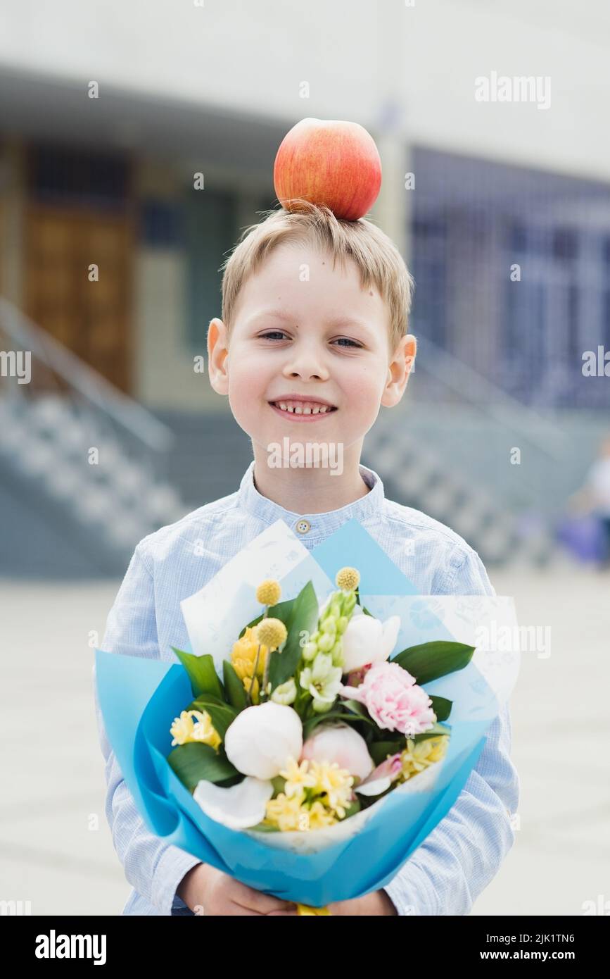 Portrait of a beautiful young first-grader with bouquet in a school ...