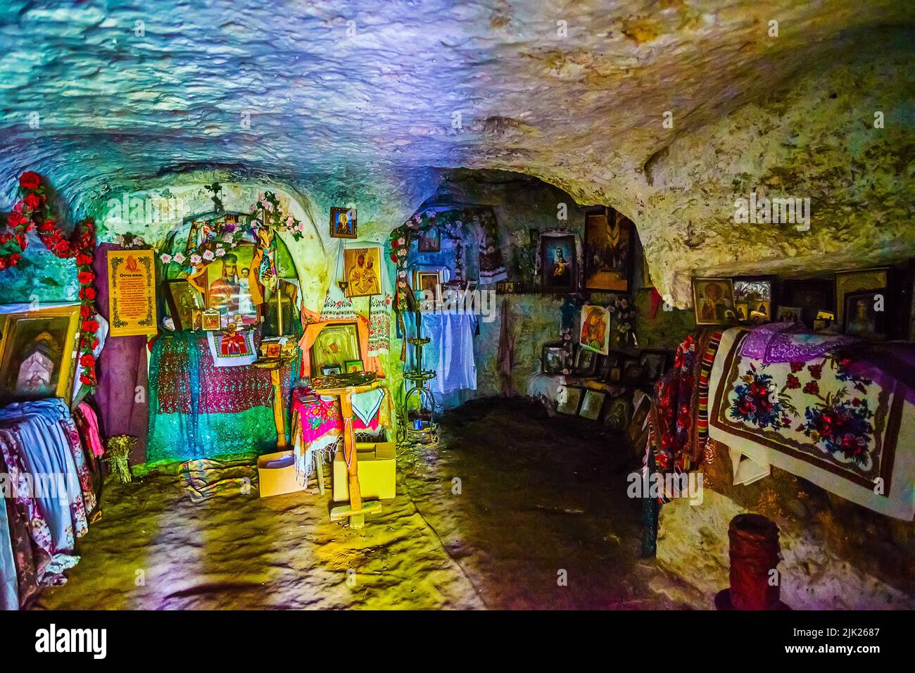 Interior of small cave chapel with altar with variety of icons of ...