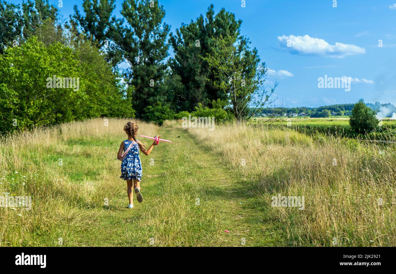 Beautiful little girl, run on the grass and launches a red toy plane ...