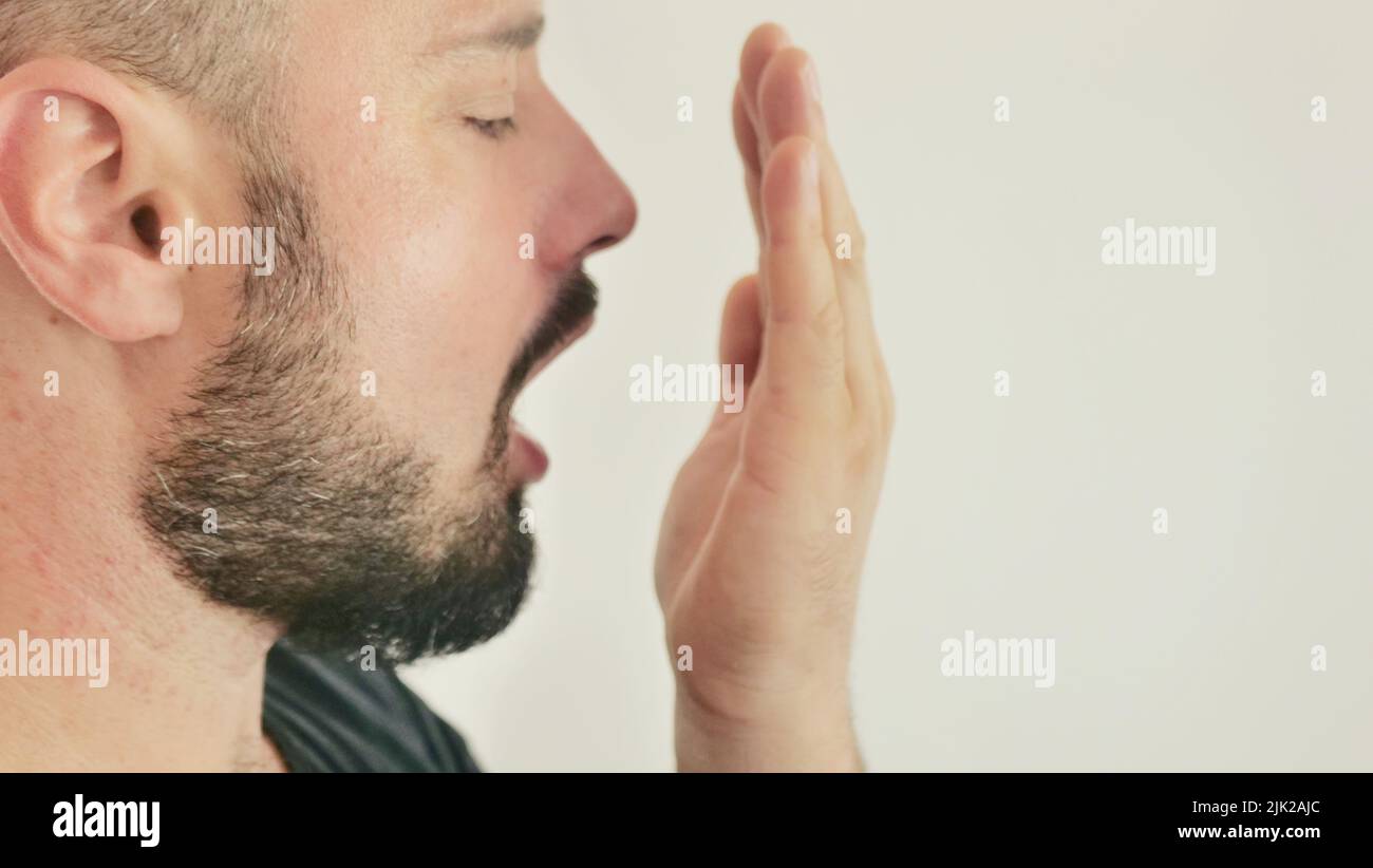 Bad breath. The concept of halitosis. A young man checks his breath ...
