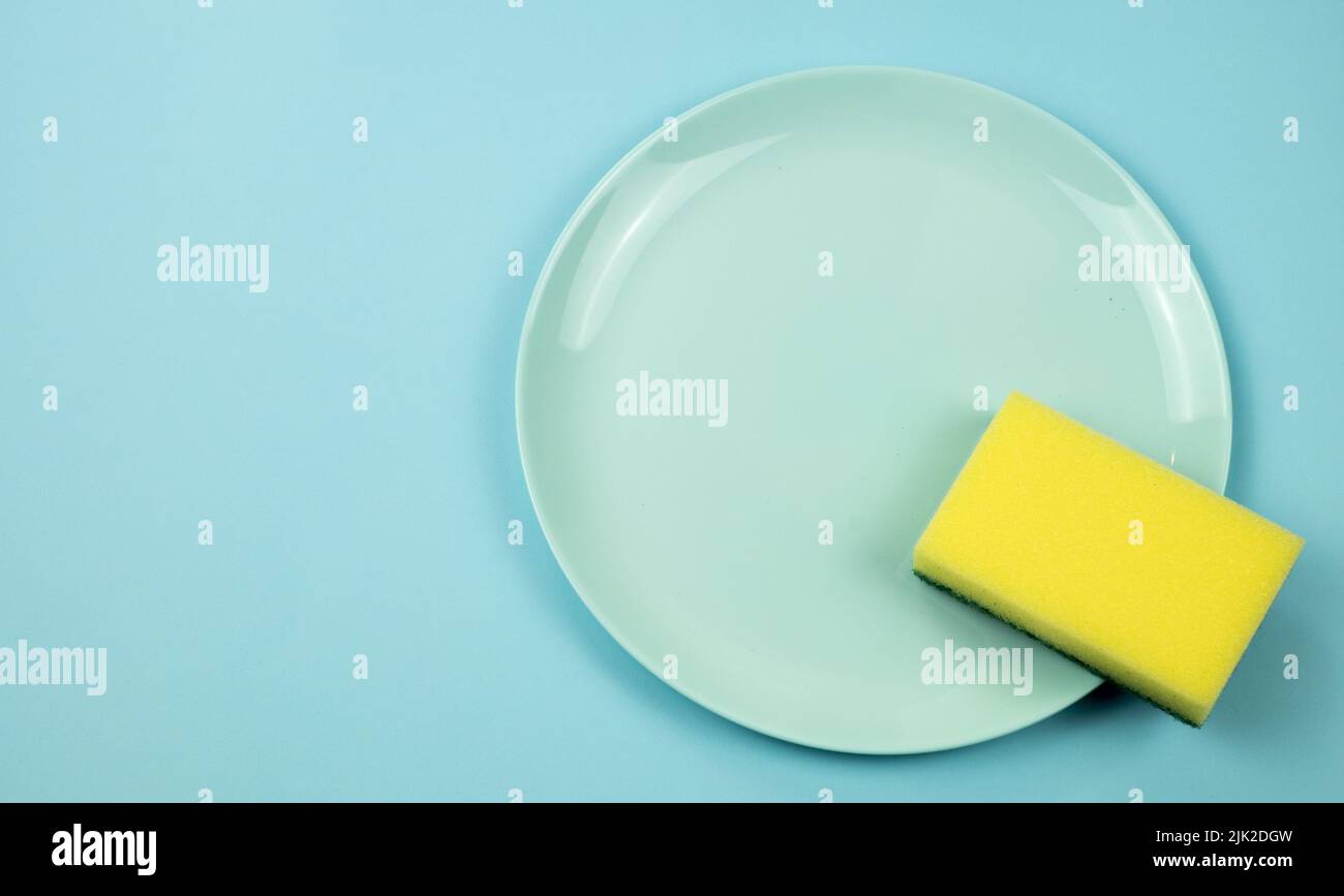 Washing dishes concept. Plate with a sponge on a blue pastel background ...