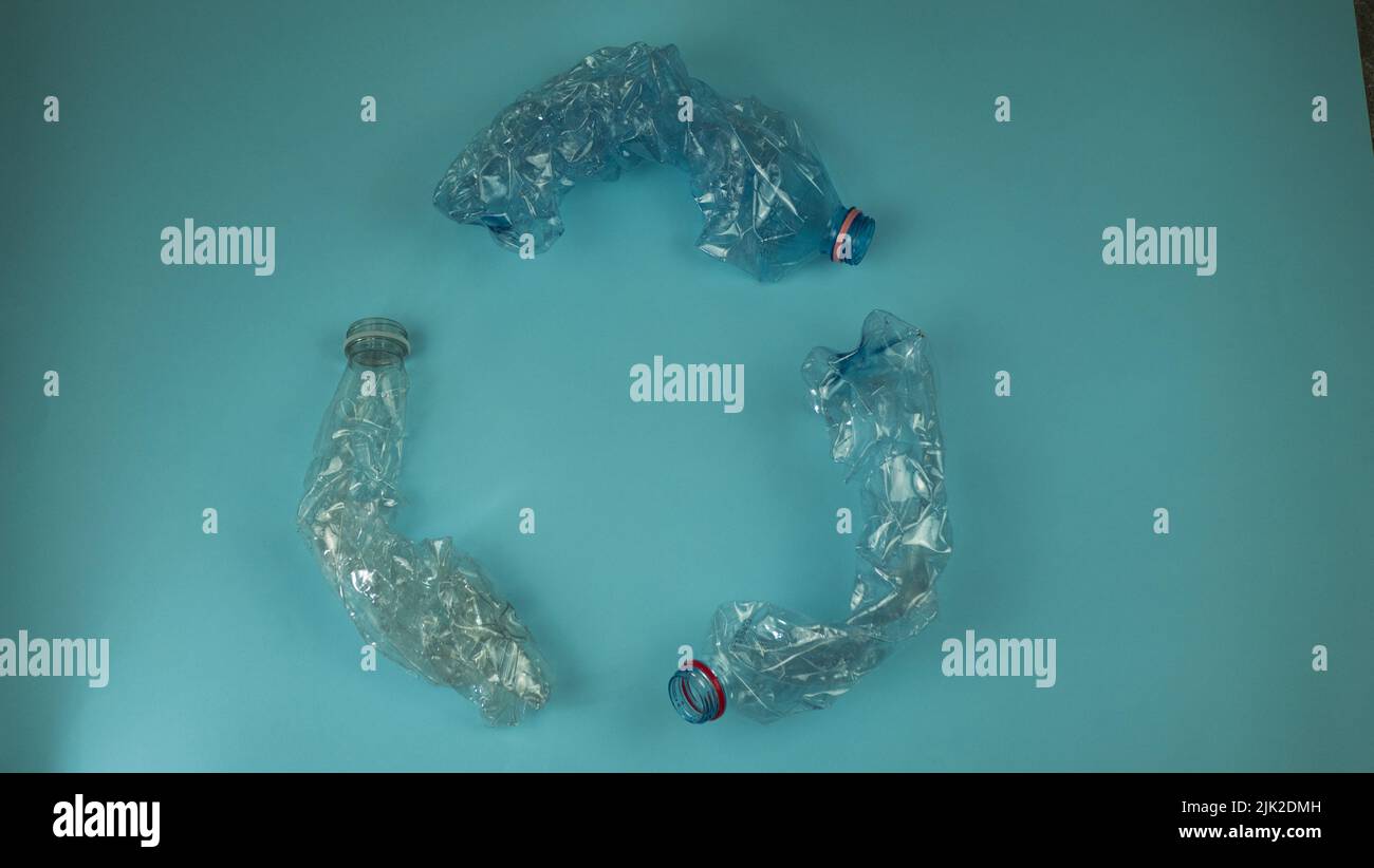 Three crashed plastic bottles on blue background form resycling sign ...
