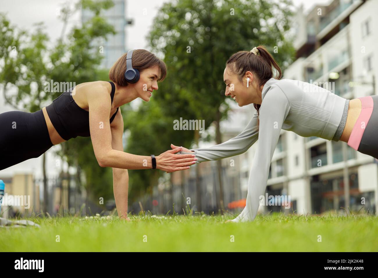 Two happy female friends holding hands while doing plank exercise in ...