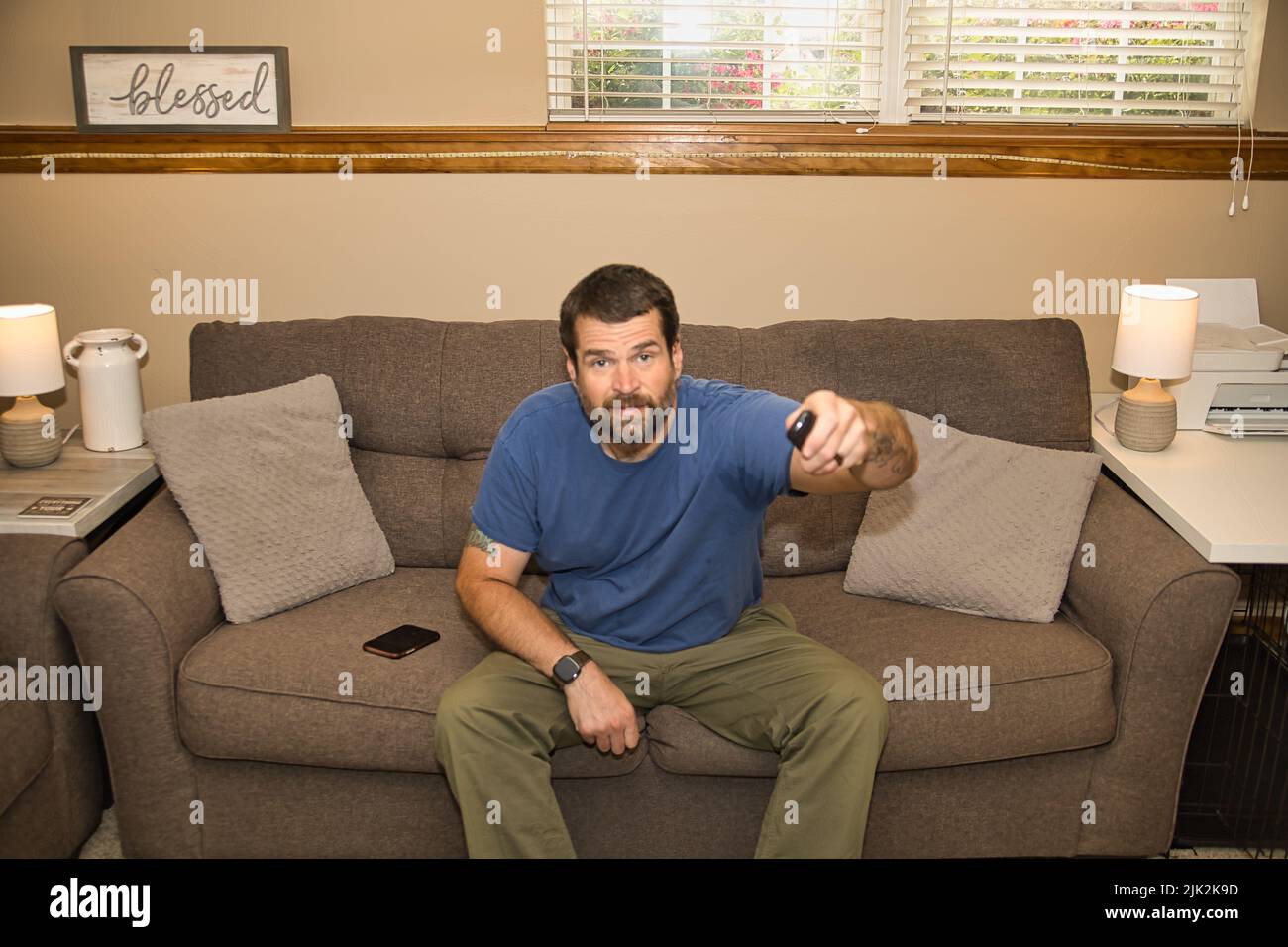 Dark Haired Bearded Man Sitting On Gray Couch Holding Tv Remote Stock