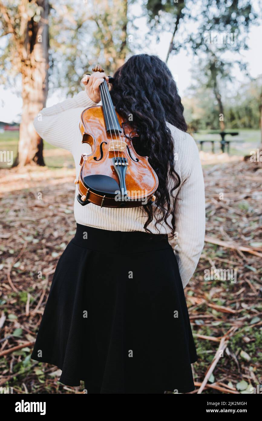 curly brunette woman holding a violin on her back, walking through the ...