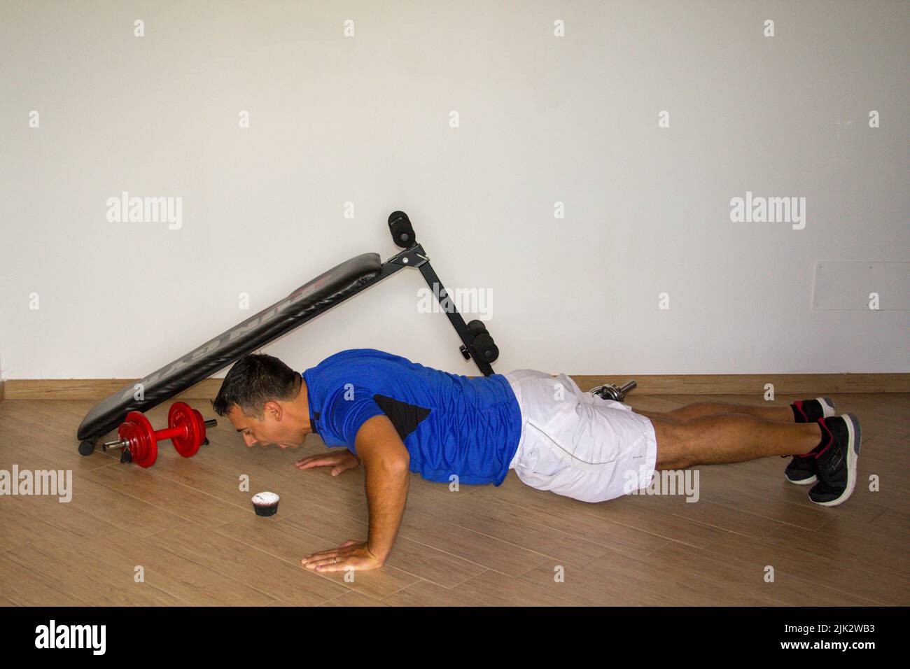 Image of a man in sports gear doing push-ups while eating a pastry ...