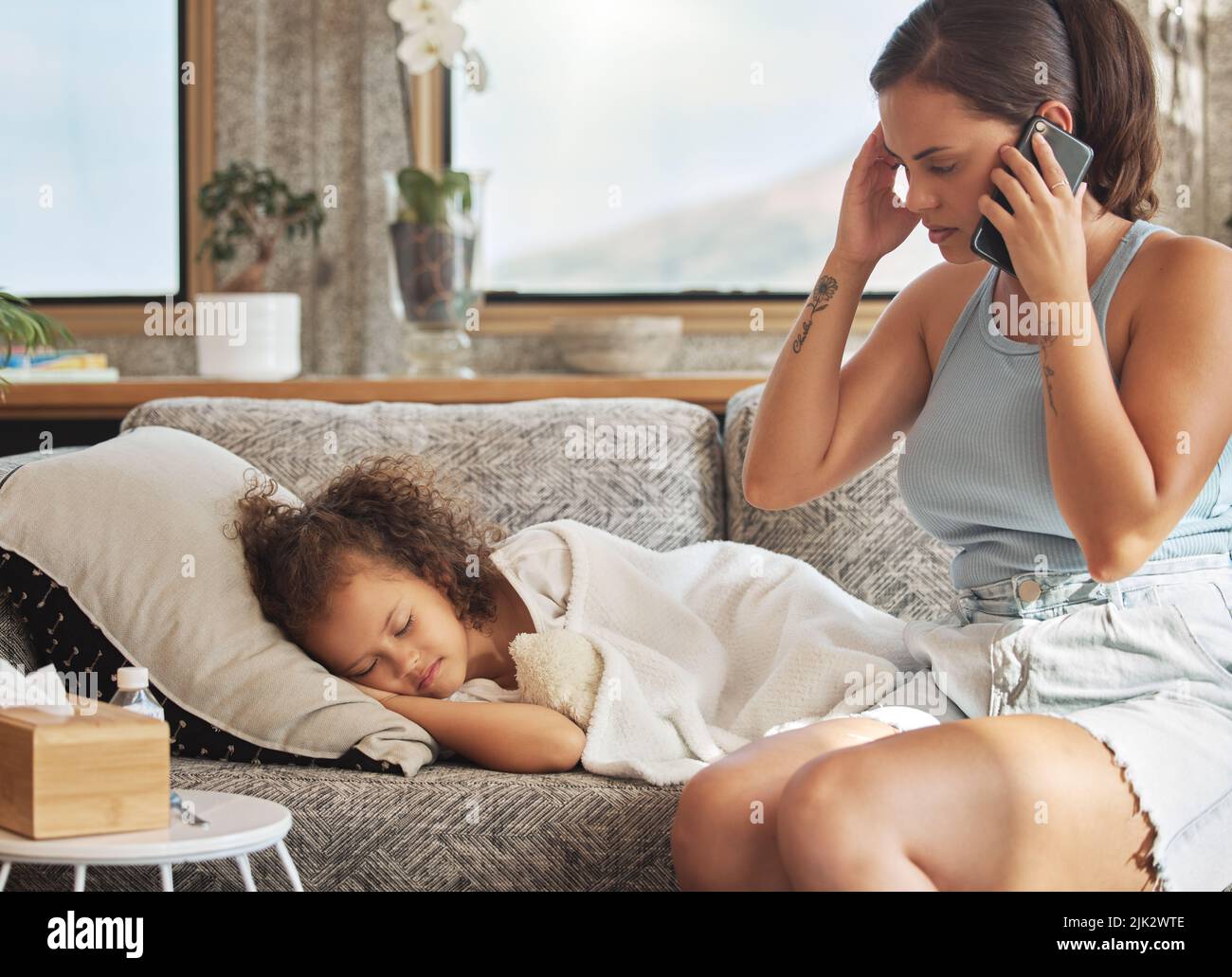 Stressed mother on a call about sick child on a sofa, worried about her ...