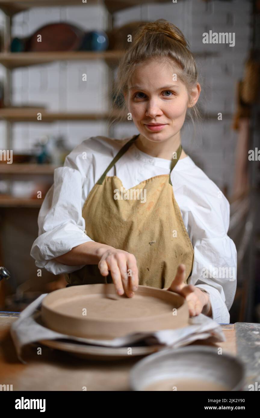 A ceramist makes a plate. Woman in an apron works in a pottery workshop ...