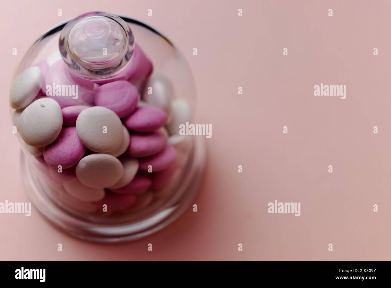 Pink and white peppermint candies in a glass jar on a pink background ...