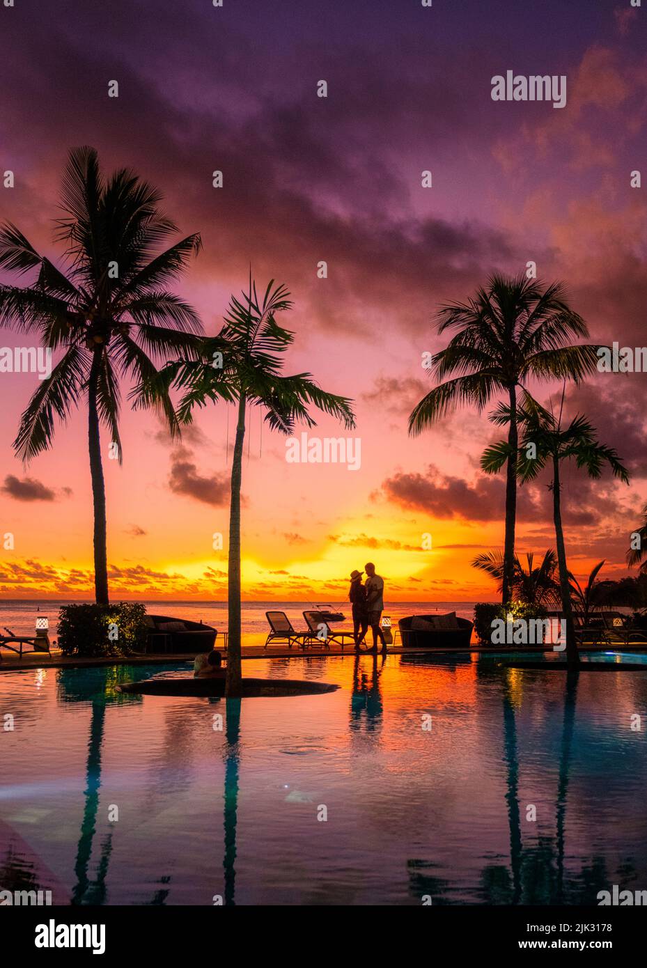 a couple of men and women watching the sunset on a tropical beach in ...
