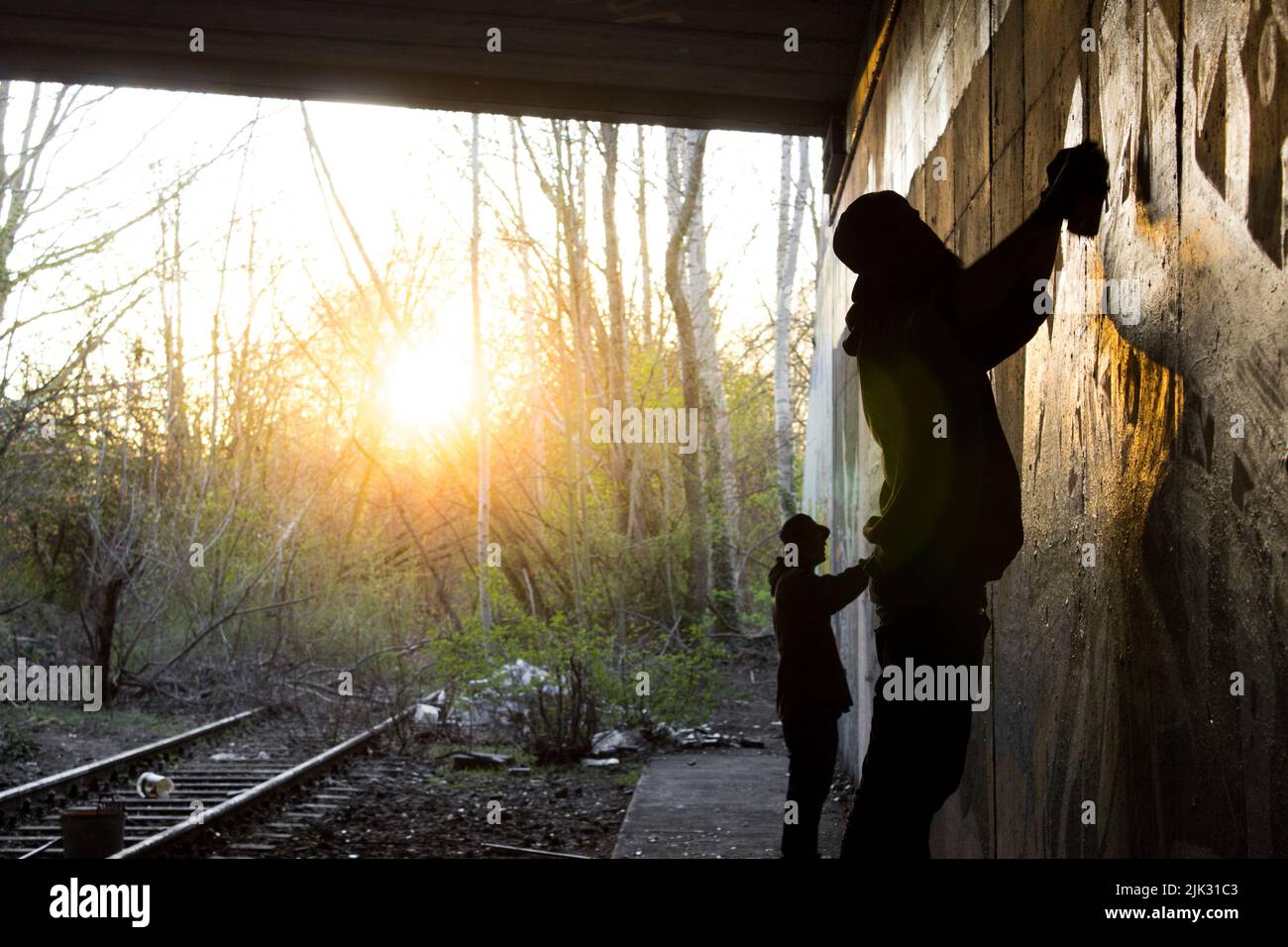 graffiti artist painting under a bridge while sunset on a wall - dark ...