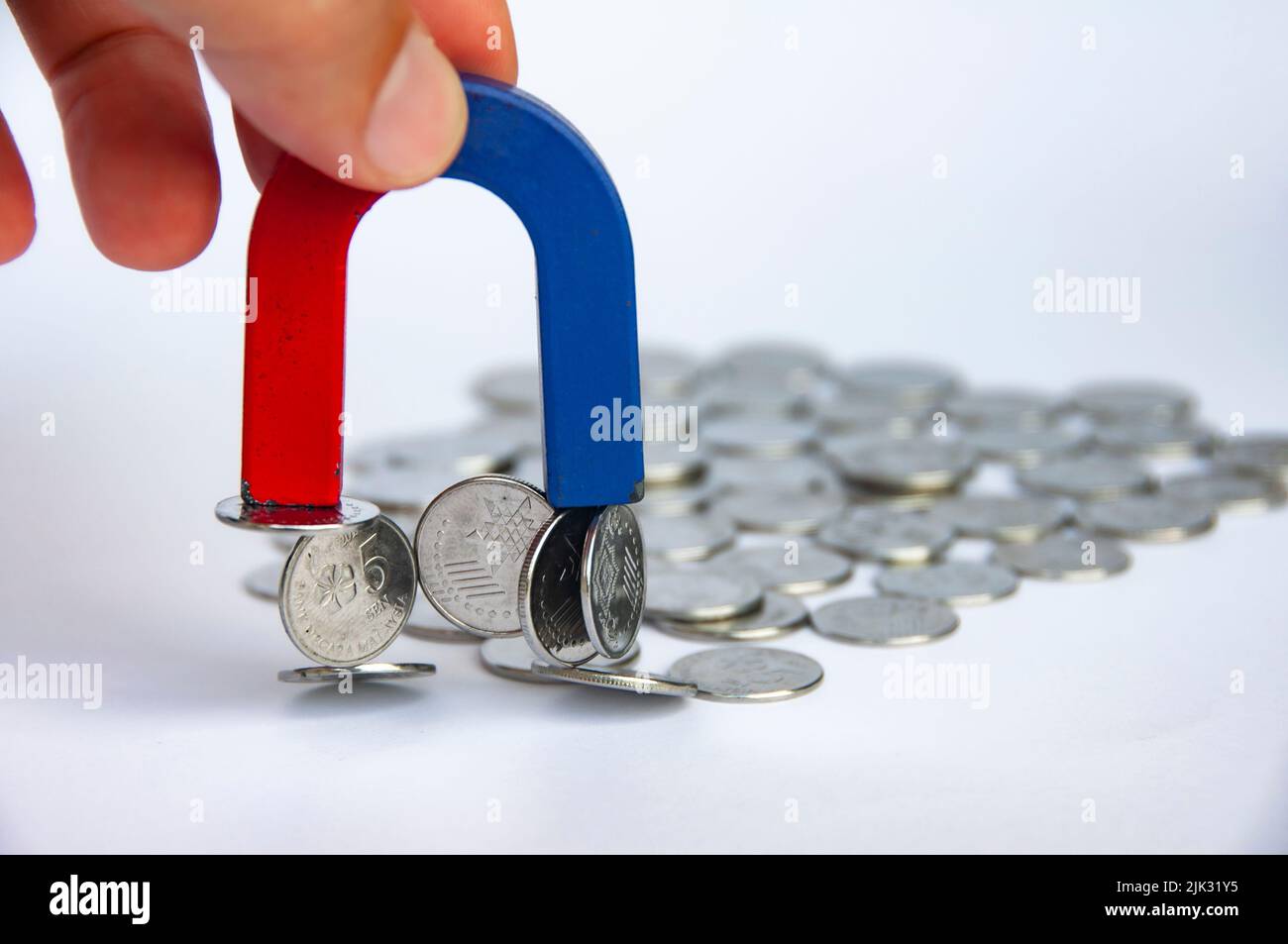 Hand holding magnet attracting silver coins with white cover background ...