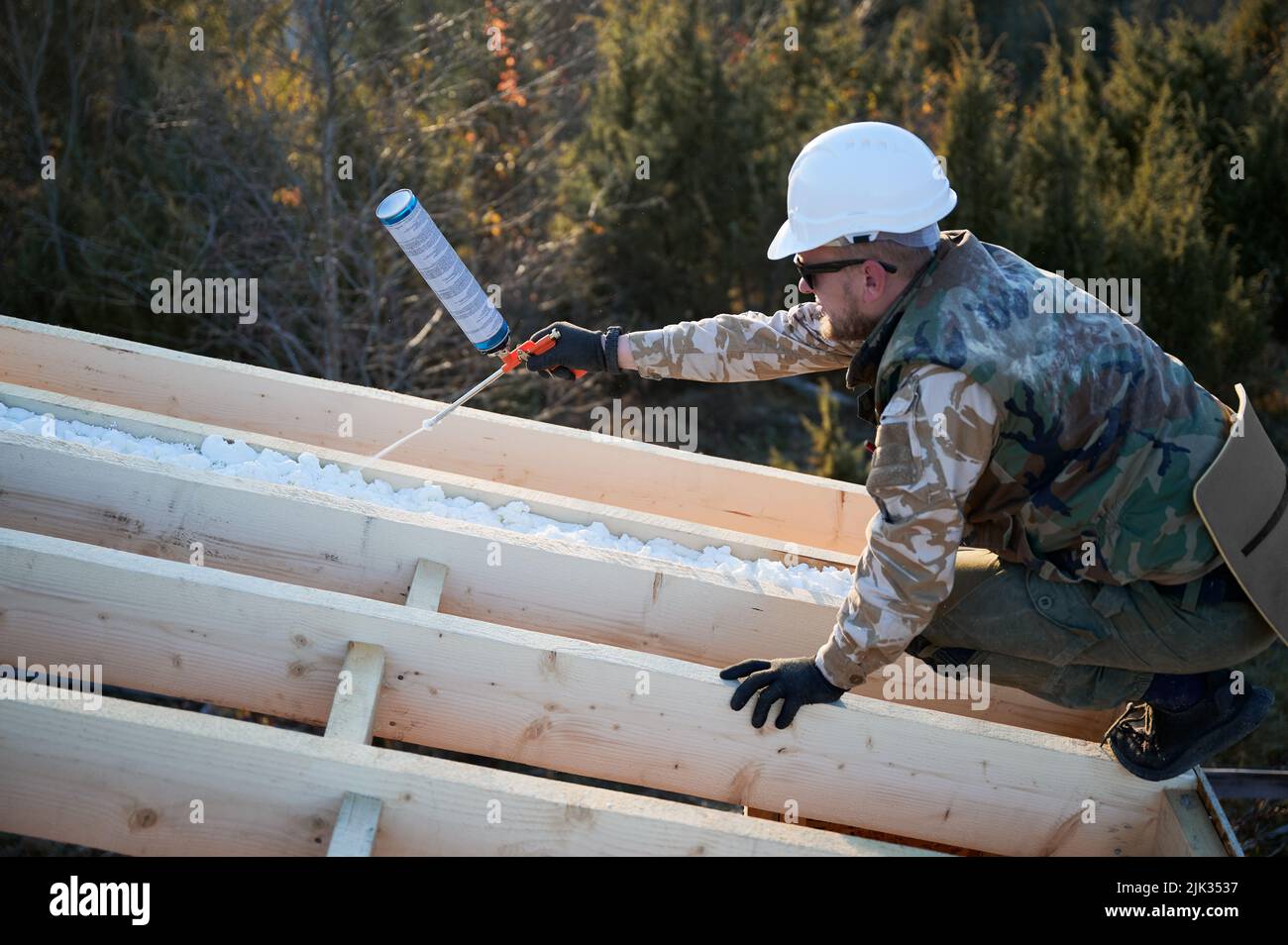 Male builder doing thermal insulation on roof of wooden frame house ...