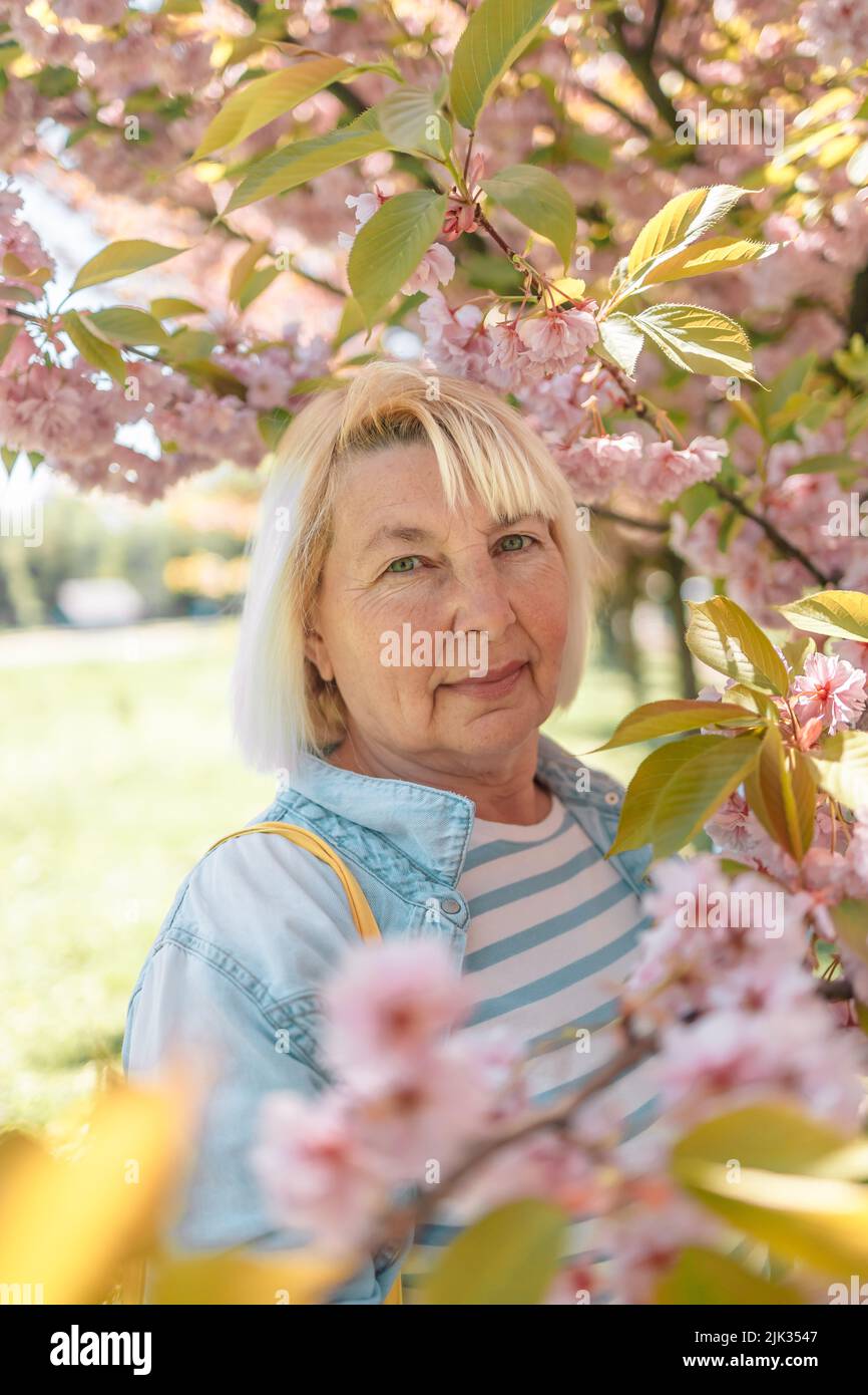 Beautiful 50s woman enjoying sunny day in park during cherry blossom ...