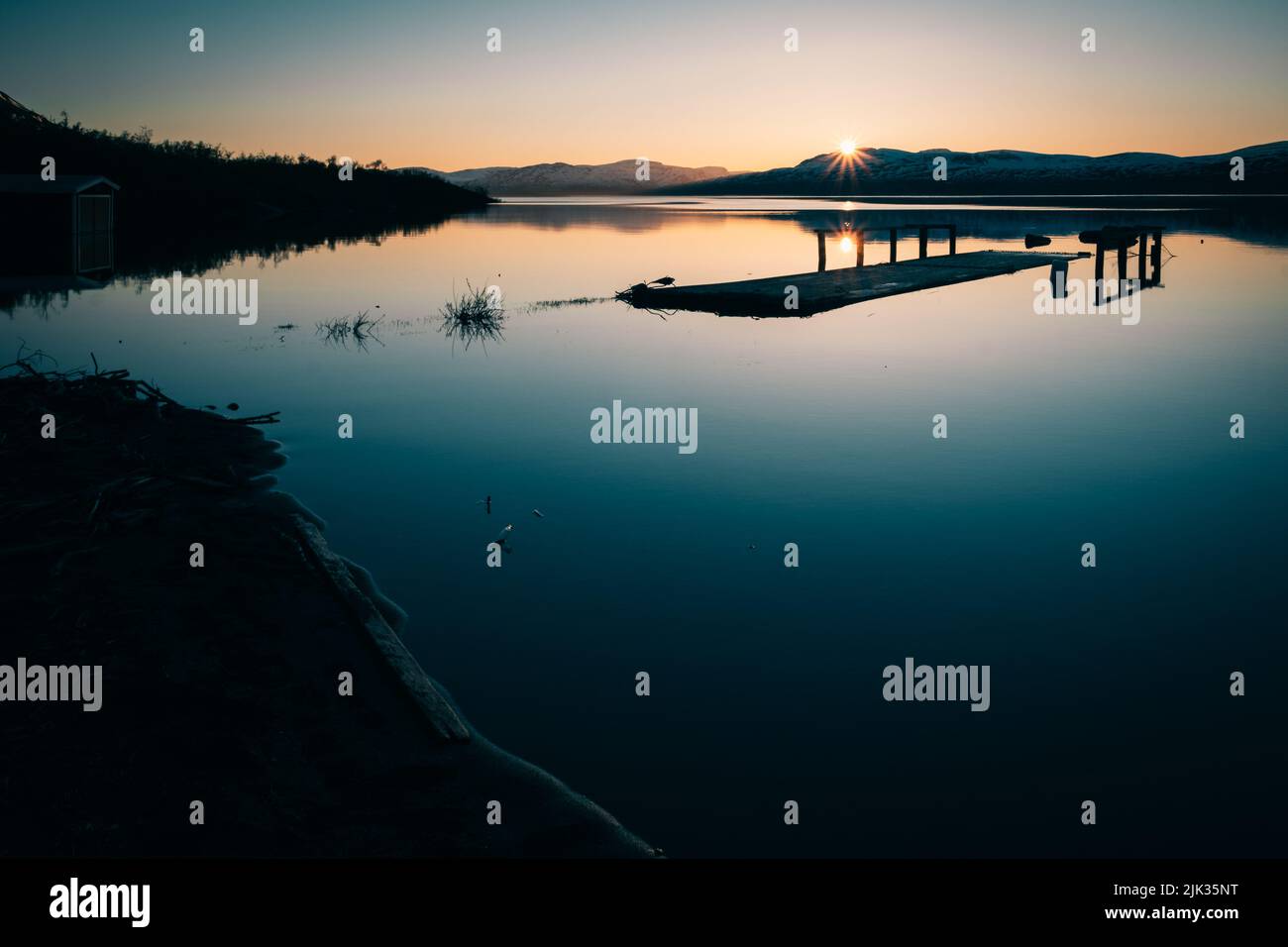 Midnight sunset over the mountains behind an arctic lake at midsummer ...
