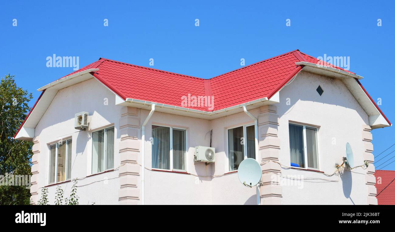 A stucco house with a red cross-hipped roof, rain gutters, soffit ...