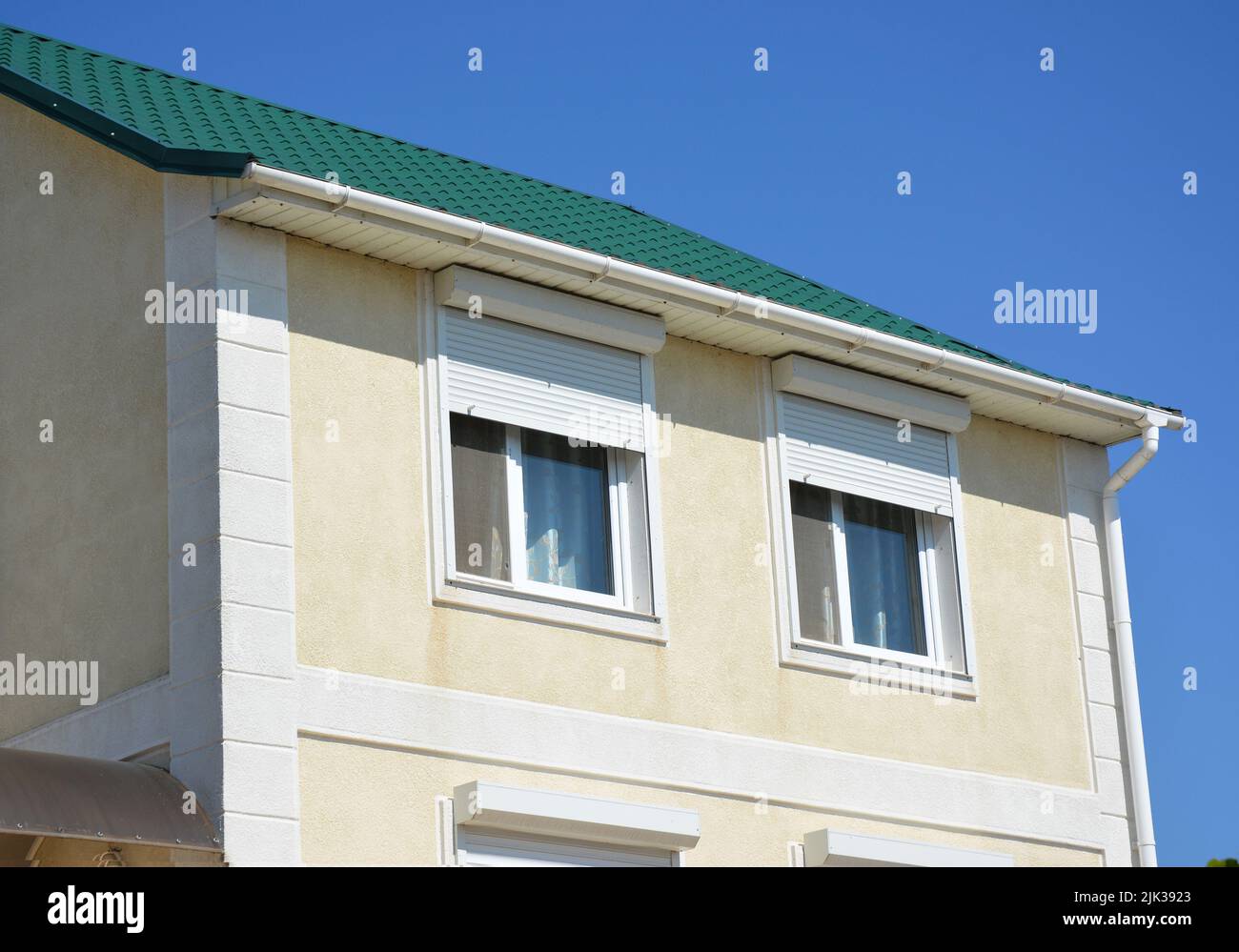 A close-up of a stucco house with a metal green roof, rain gutters ...