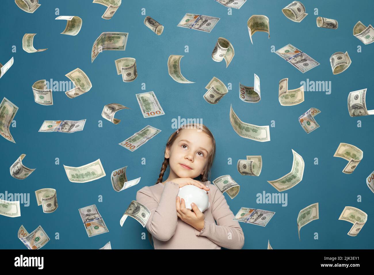 Happy attractive little kid on falling money rain on blue background ...