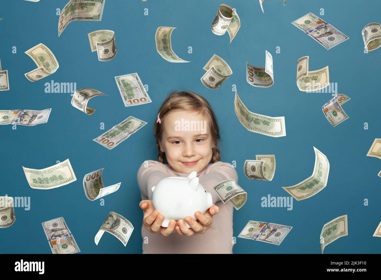 US dollar money rain and piggy bank in hand of cute child girl on blue ...