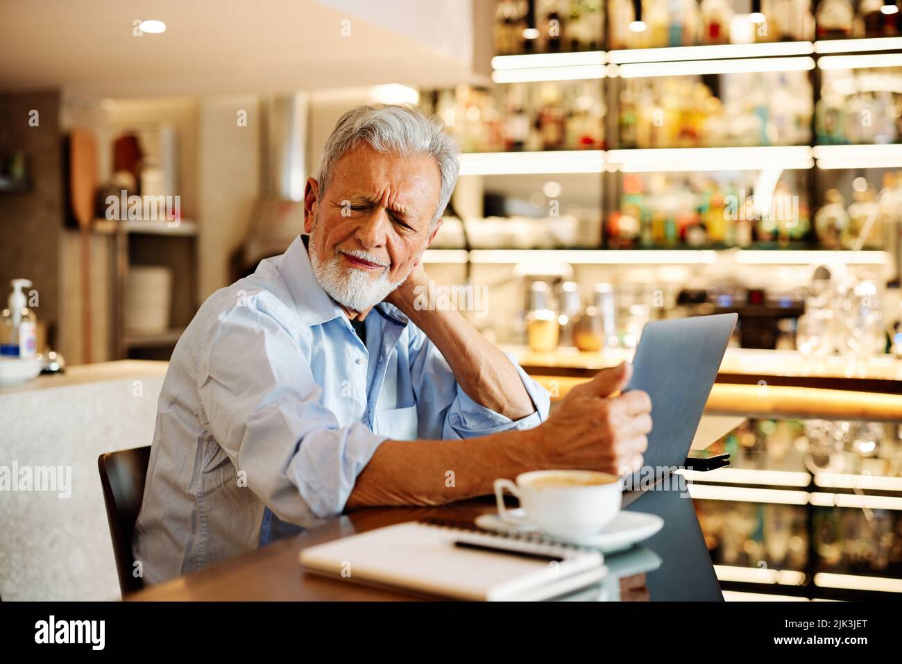 A senior student is sitting at home and rubbing his neck. He is tired ...