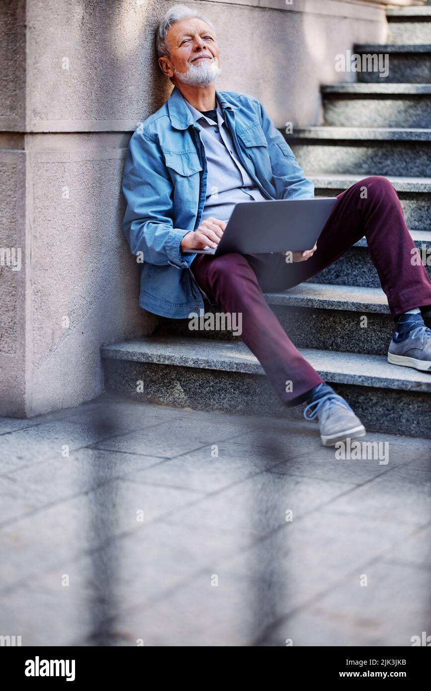 A senior student sits on the stairs of the university building and uses ...