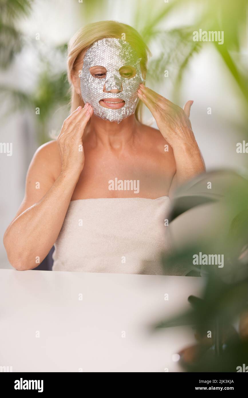 A senior woman putting beauty face mask on her face, while sitting at ...