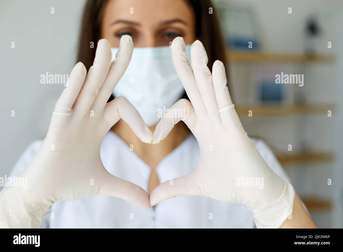 Female MD in medical gown showing heart symbol by palms, standing ...