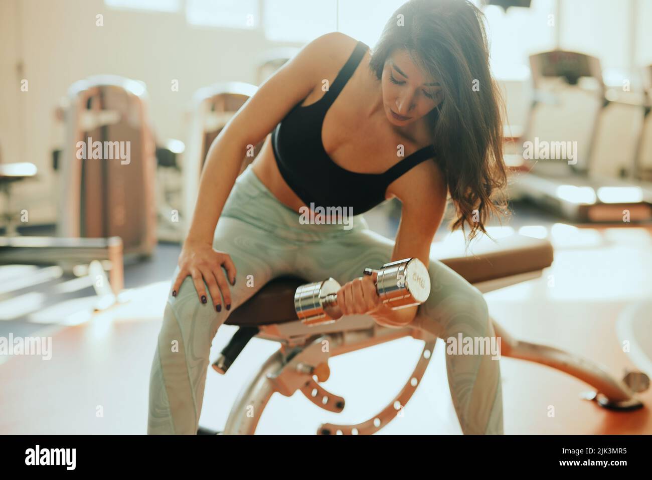 A strong bodybuilder is leaning on a bench in a gym and doing workouts ...
