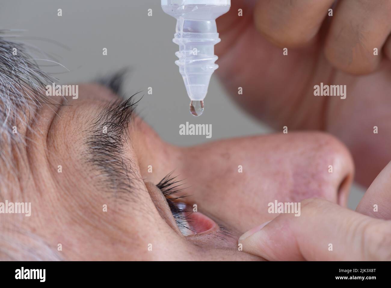 Close-up view of a senior Asian adult male using eye drop in right eye ...