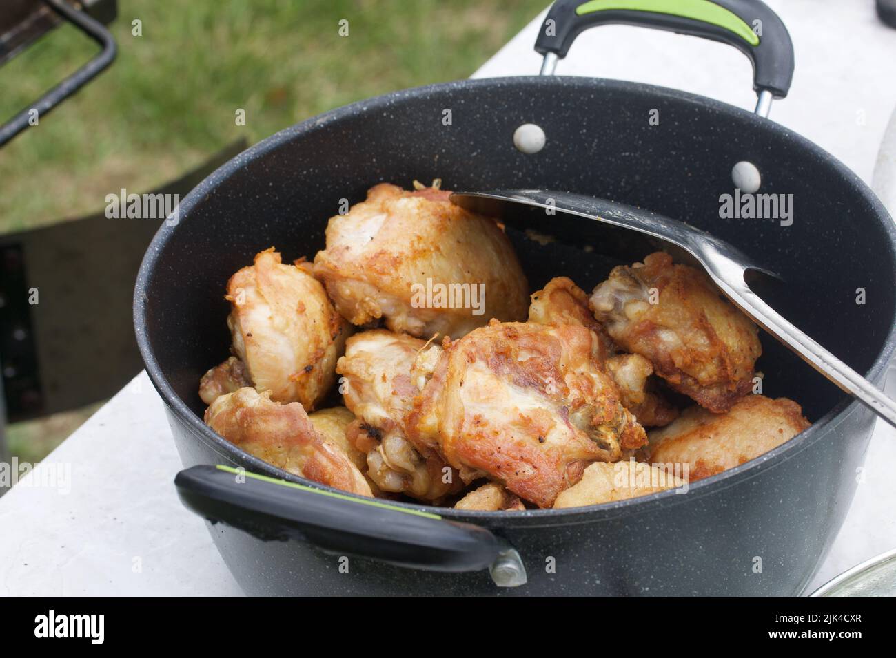 Chicken thighs are fried in a cast-iron cauldron. Cooking outdoors ...
