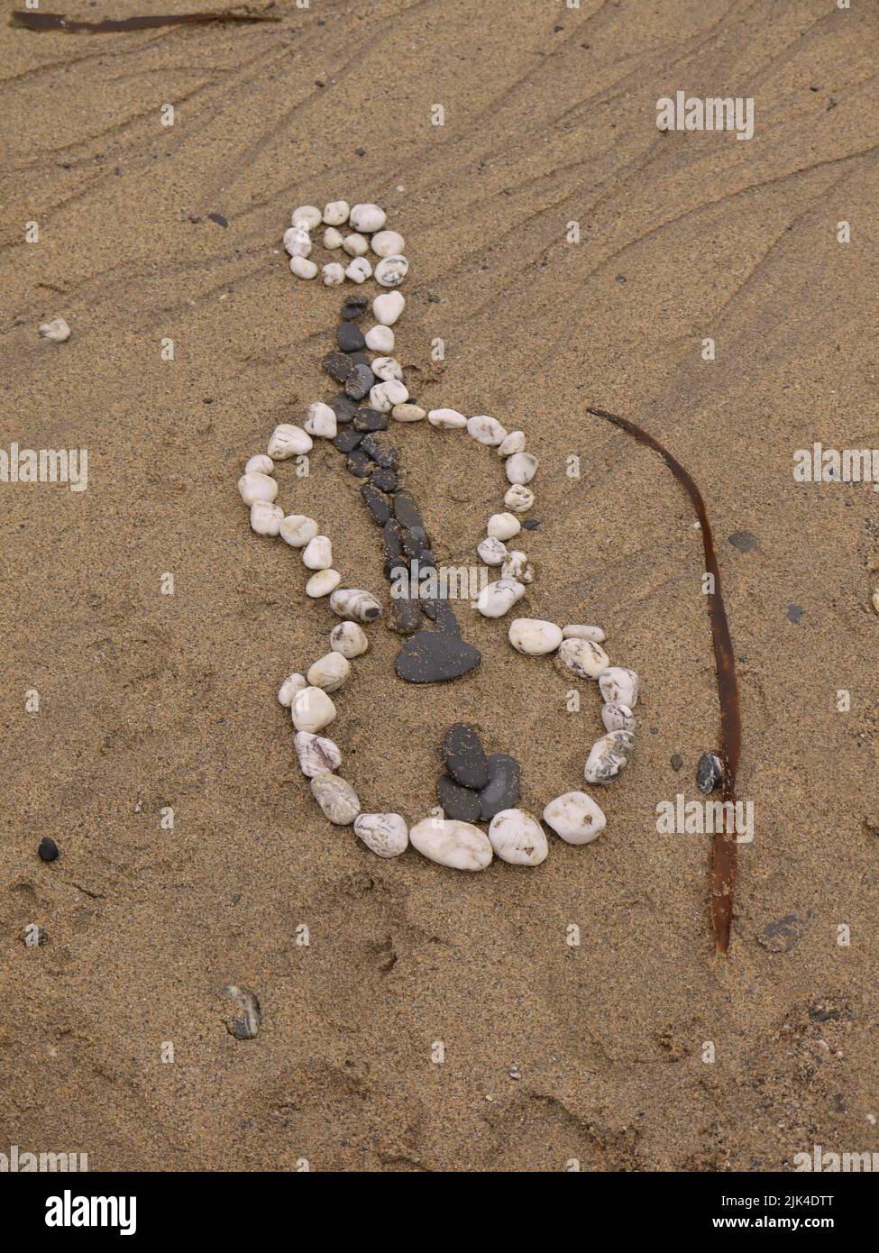 Vertical shot of a pebble violin with a seaweed bow on a sandy beach ...