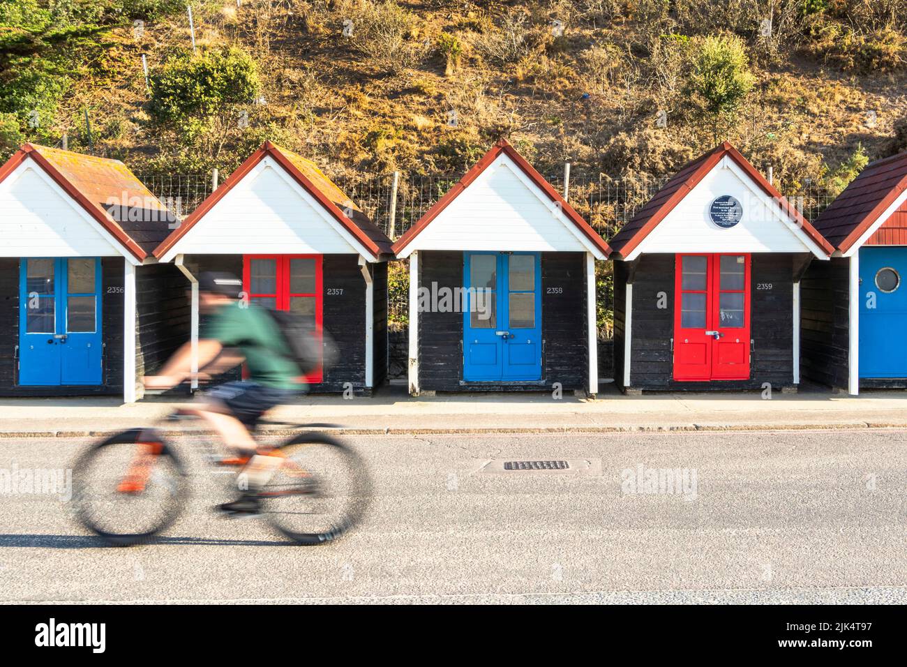 row of red and blue wooden beach huts with blurred passing cyclist ...