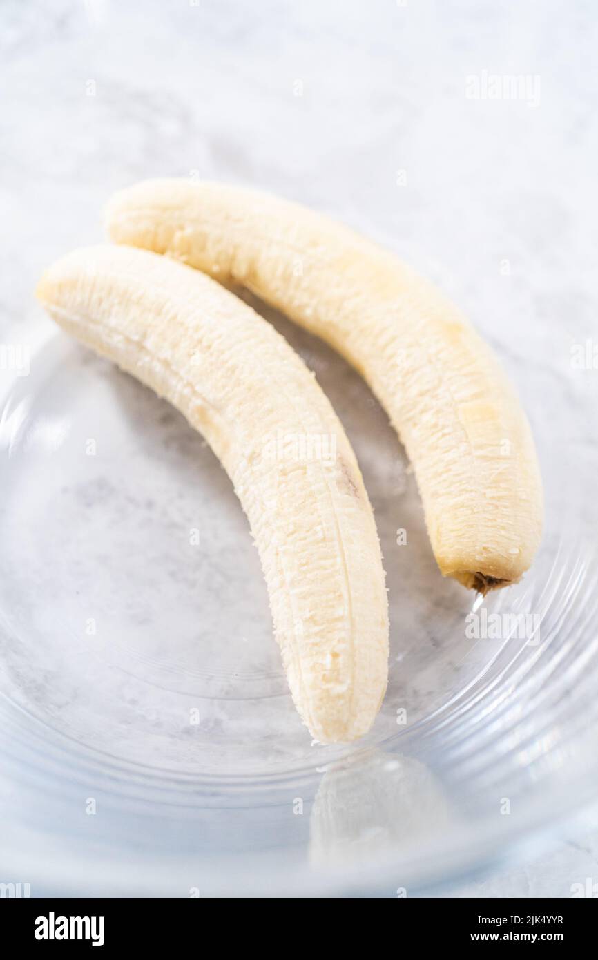 Smashing riped bananas in a glass mixing bowl to prepare coconut banana ...