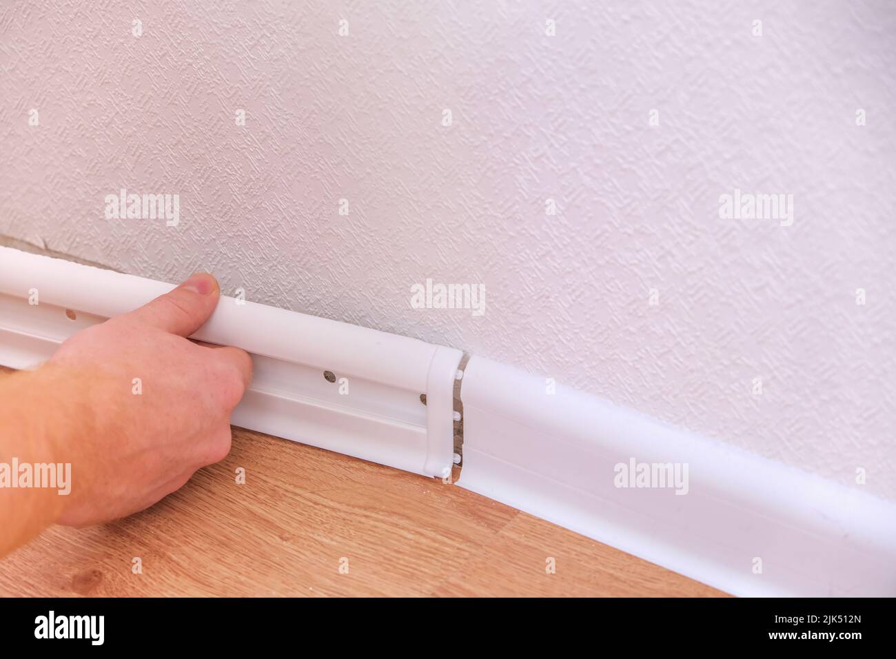 A man installs a floor skirting board. Fixing the plastic skirting ...