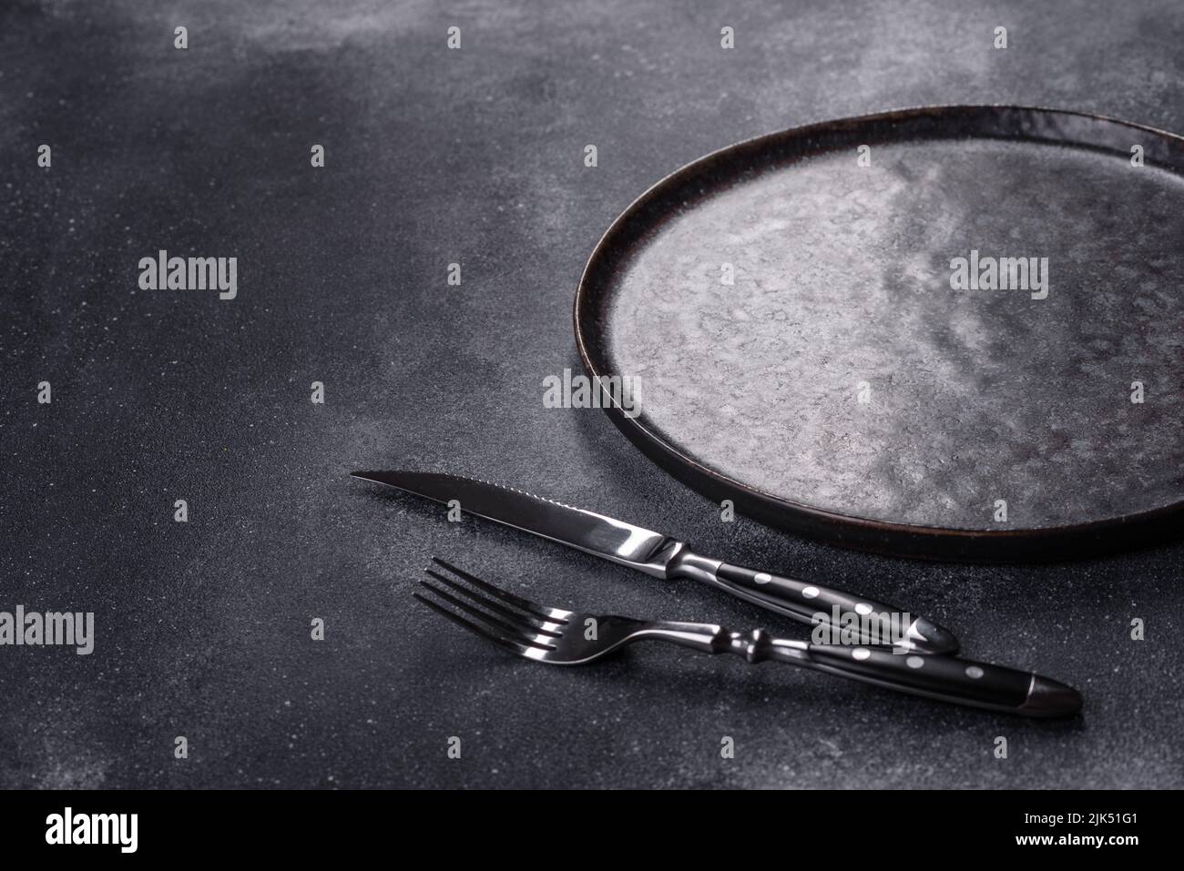 Empty black plates, fork and knife on a gray background. Top view, copy ...