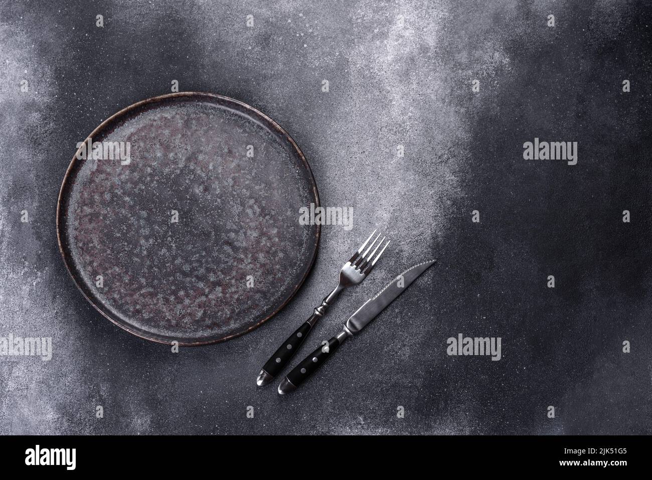 Empty black plates, fork and knife on a gray background. Top view, copy ...
