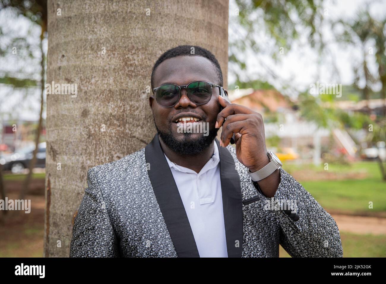 Young smiling black man on vacation, leaning against a tree makes a ...