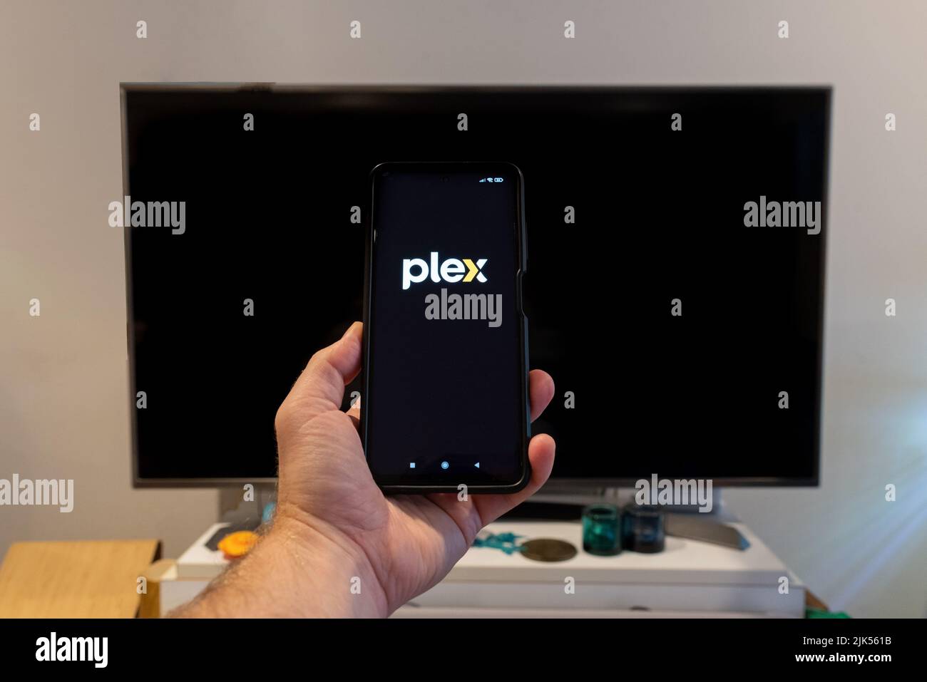 hand hold up an illustration of the plex logo displayed on a smartphone ...