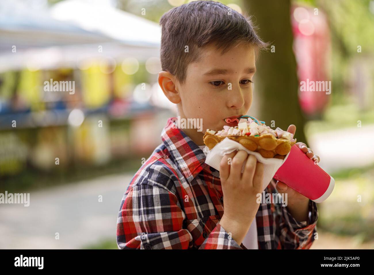 Small Caucasian boy eating sweet waffle at street. Child with fast food ...