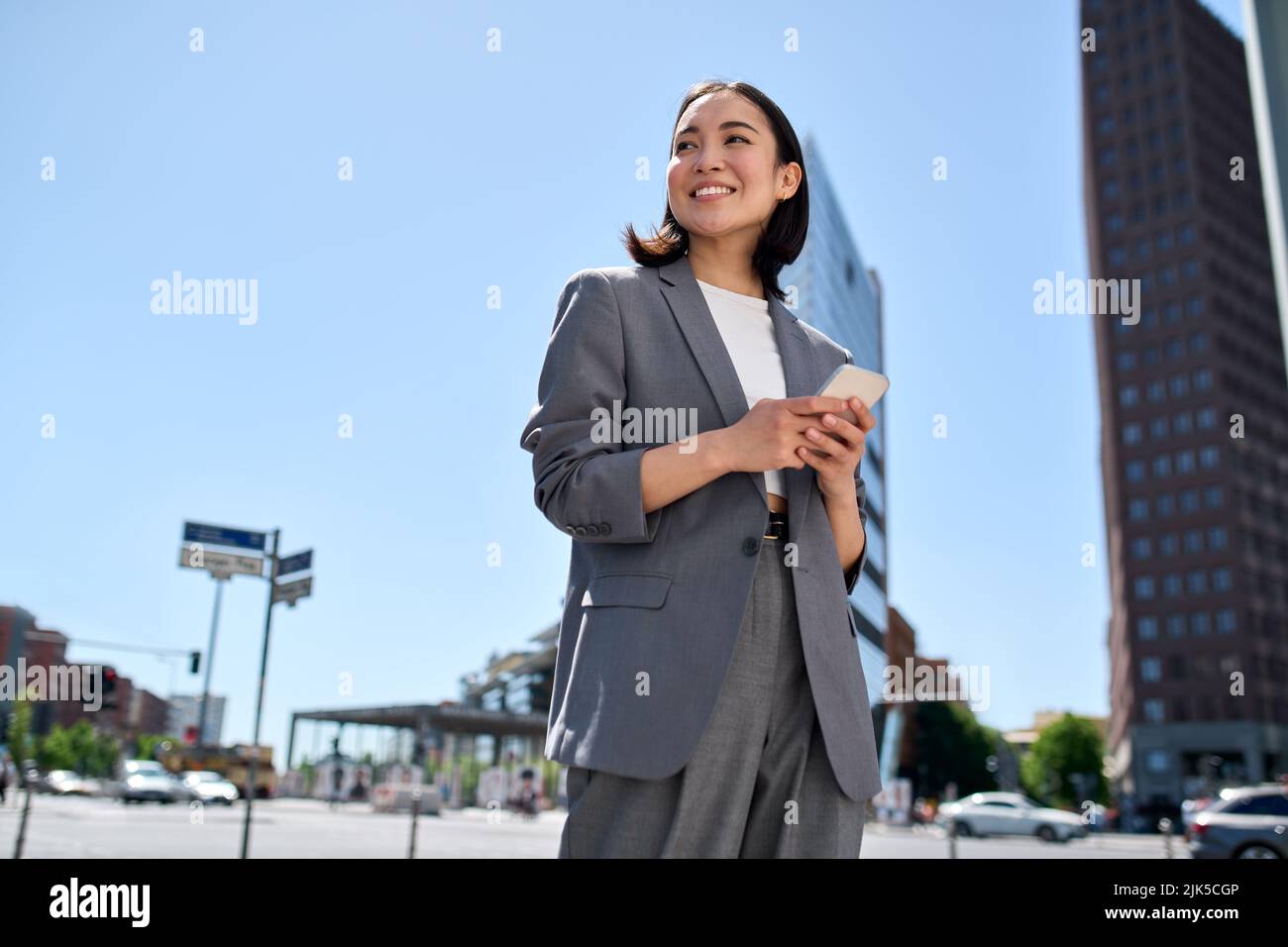 Young successful Asian business woman using phone standing on city ...