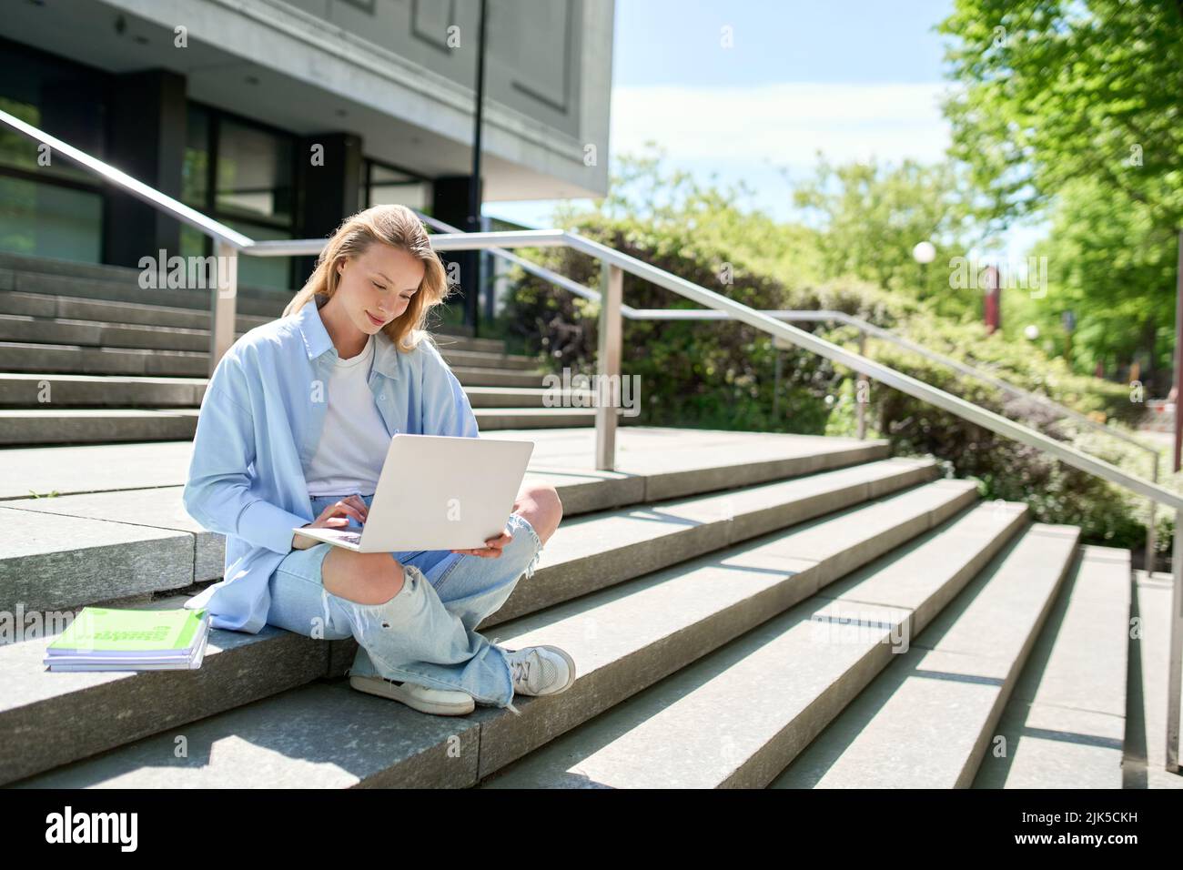 Smiling girl student using laptop computer outdoor in university campus ...