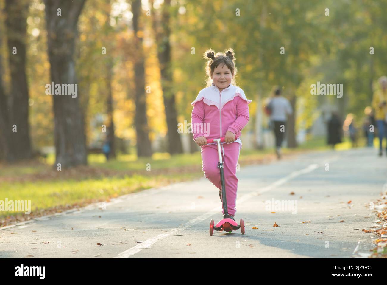 A little girl in pink costume riding a small kids scooter in autumn ...