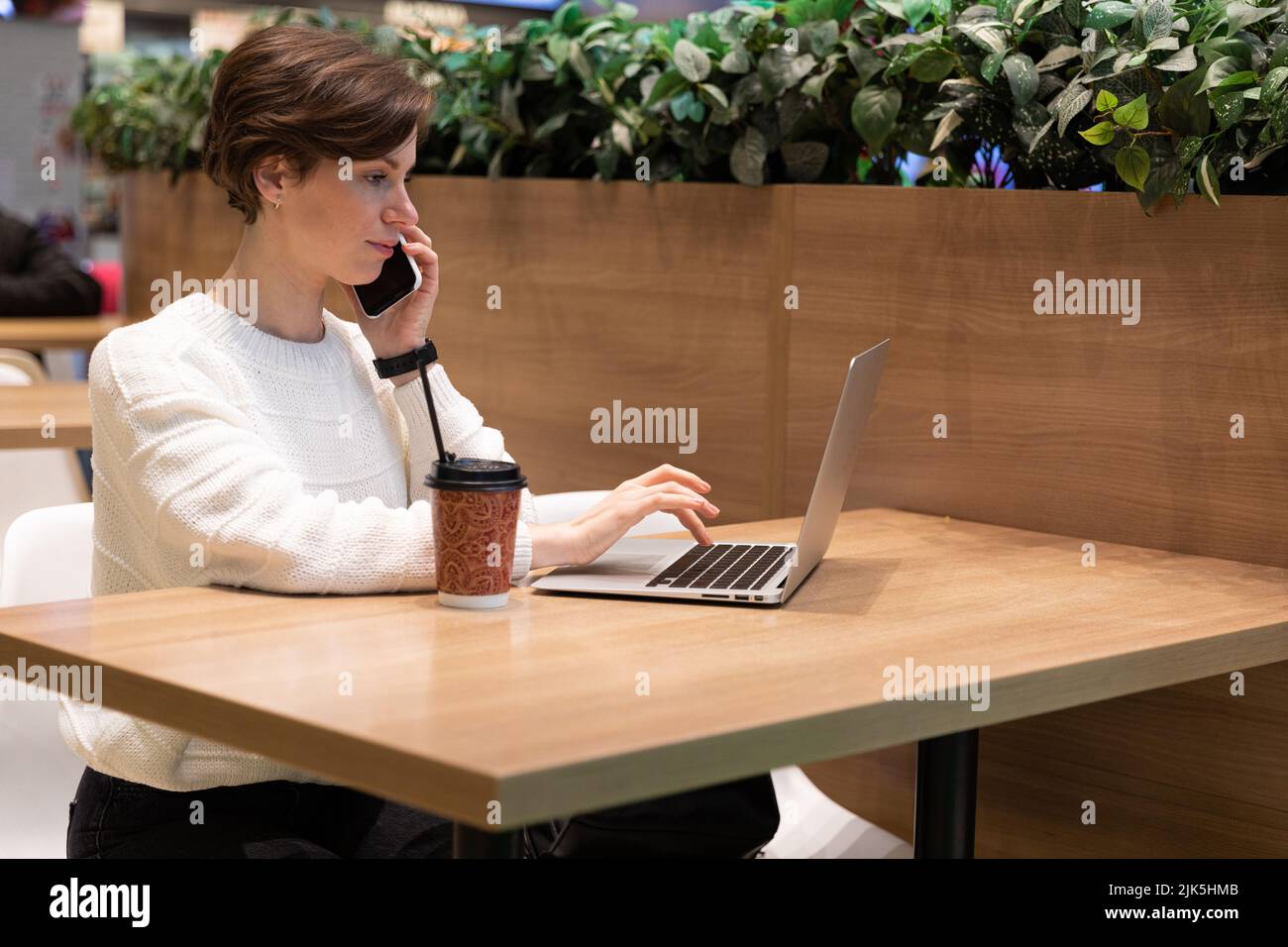 young woman sitting at the table talking on the phone typing something ...