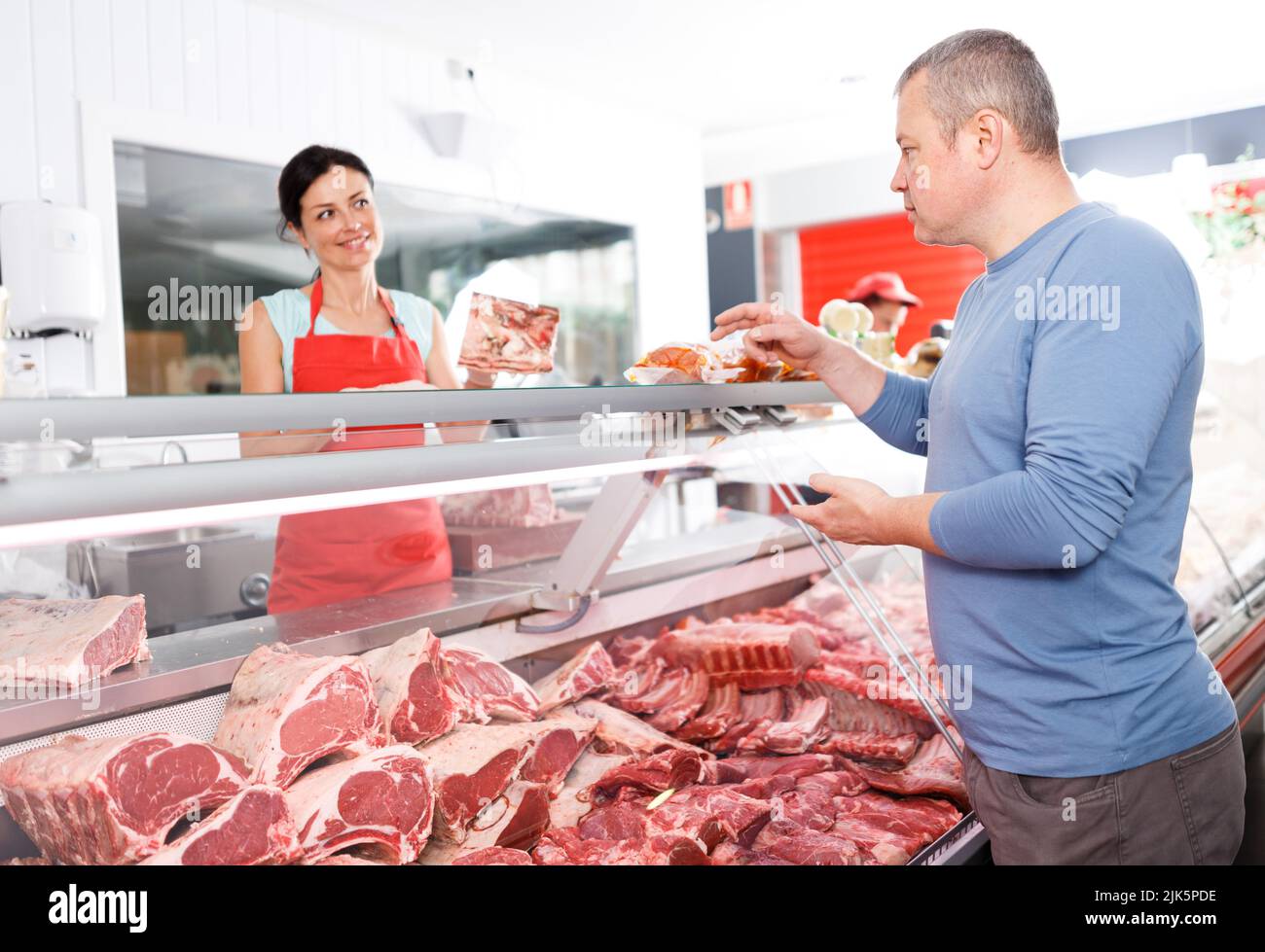 Female seller helping male choosing meat in shop Stock Photo - Alamy