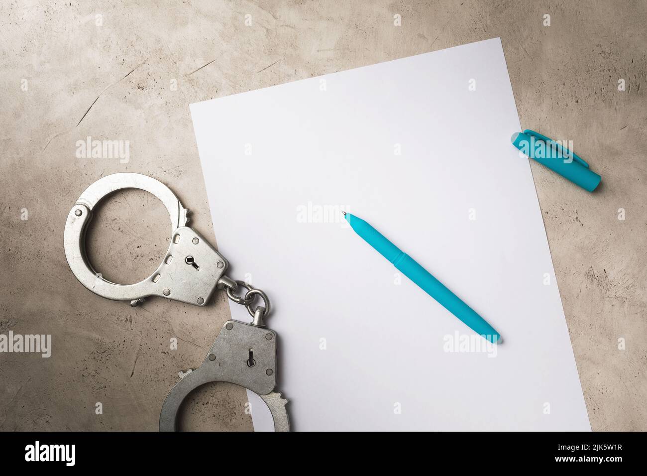 Handcuffs, an empty sheet of paper and a pen on the table Stock Photo ...
