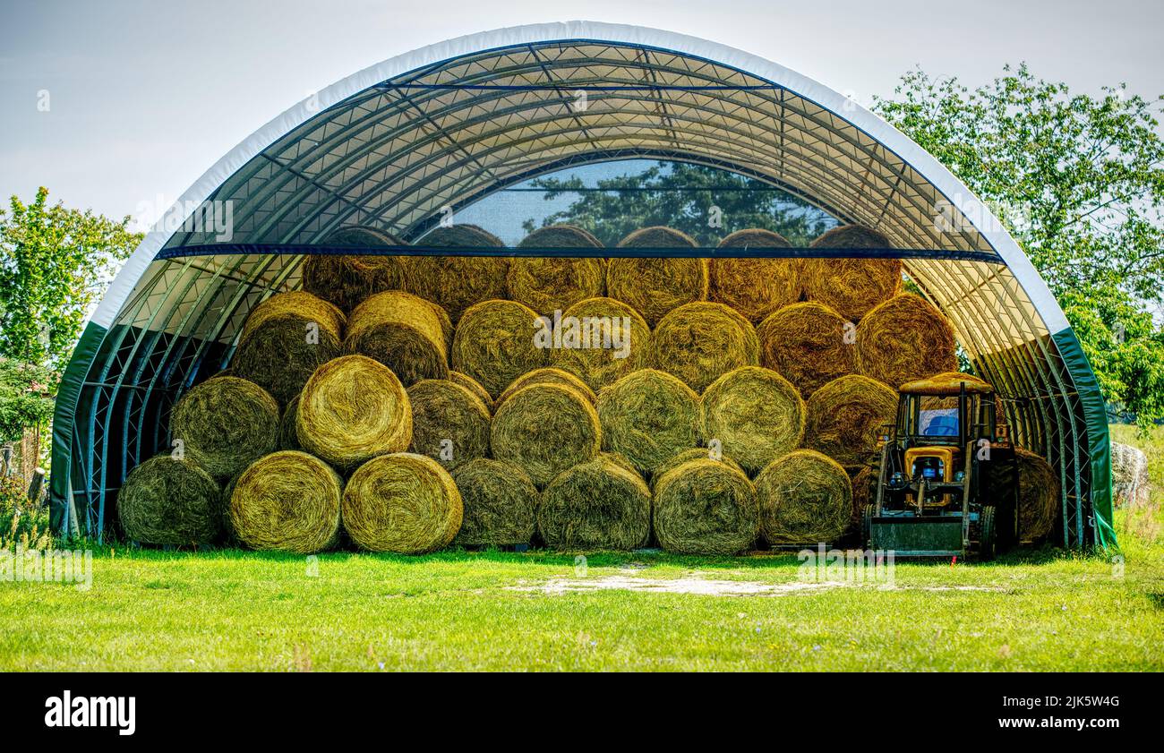 Rolled hay and tractor under the roof structure Stock Photo - Alamy
