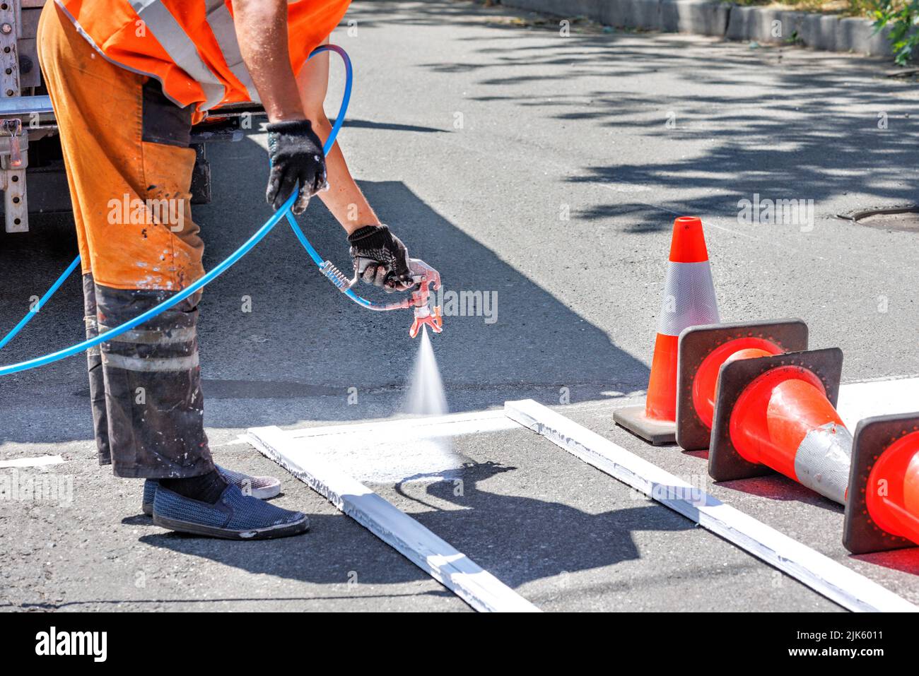 A road worker paints a white road marking of a pedestrian crossing with ...