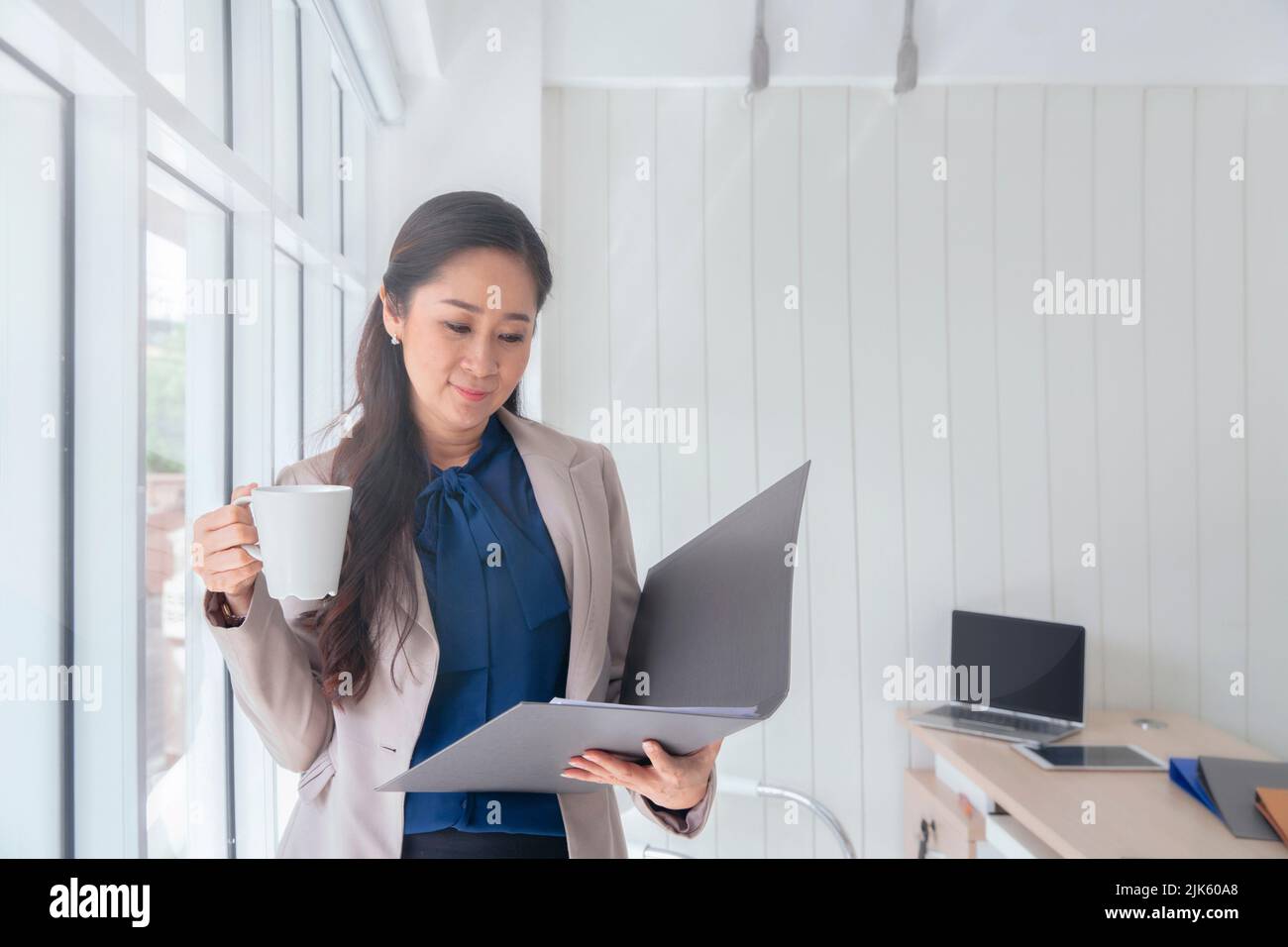Business woman drinking cup of coffee and standing at a window in ...