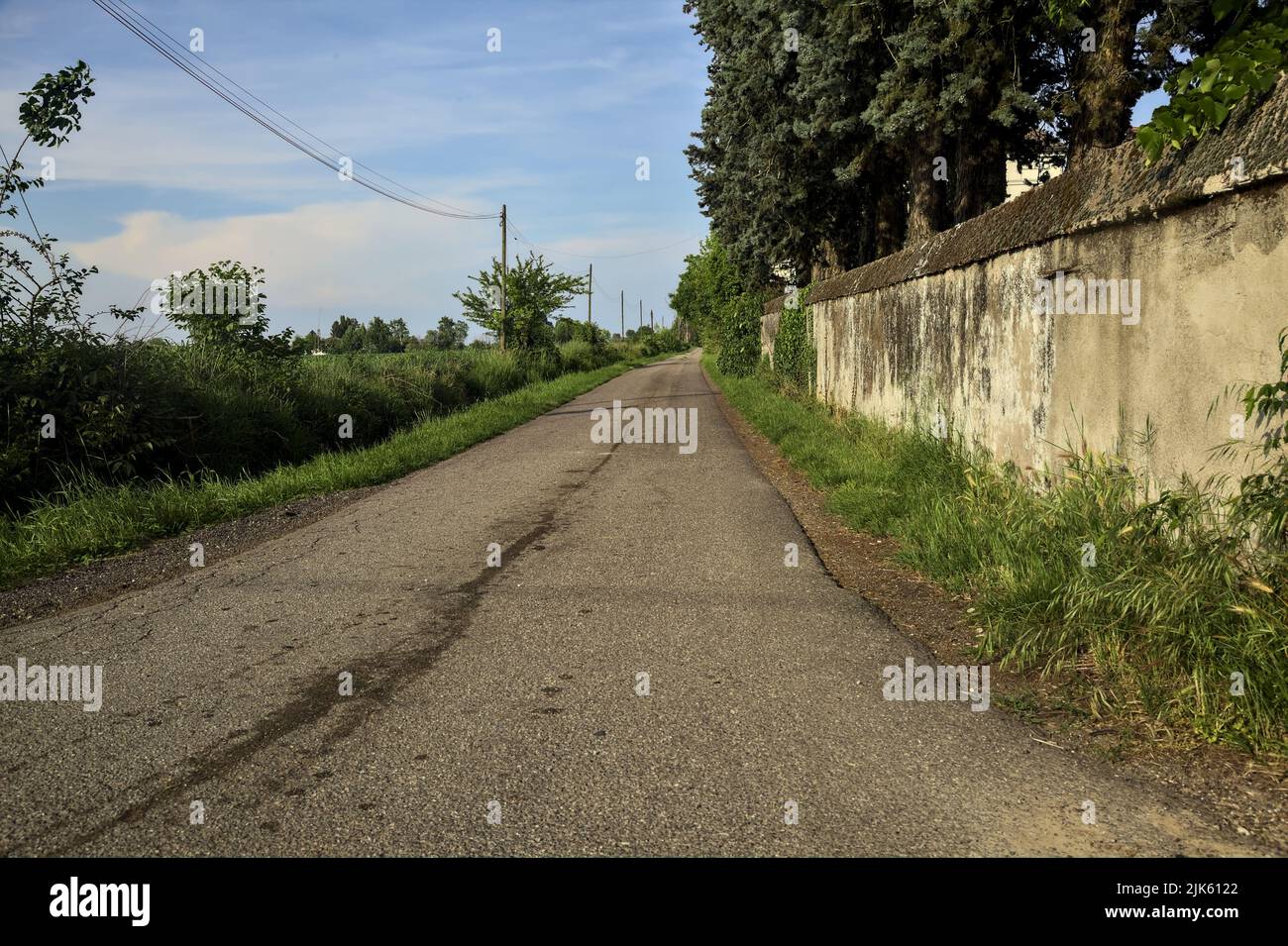 Road bordered by boundary wall and a stream of water next to a field on ...