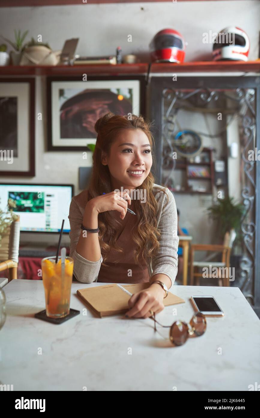 Happy Vietnamese young woman sitting in cafe and writing her ideas in ...